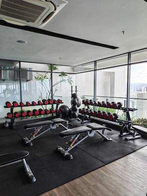 Academia moderna com diversos equipamentos de exercício, janelas amplas e vista para a cidade.