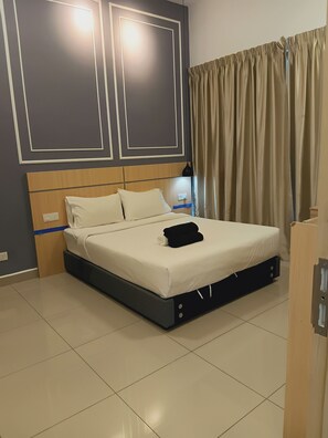 Cama bem arrumada com colchão e travesseiros brancos, cabeceira de madeira, mesa de cabeceira com abajur e cortina na janela.