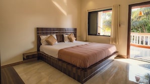 Quarto com cama grande, cabeceira de madeira, janela com cortinas e vista para o verde lá fora.