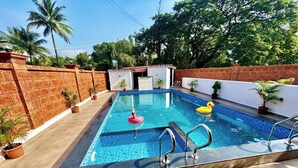 Piscina retangular com borda revestida, rodeada por um muro de tijolos e plantas em vasos.