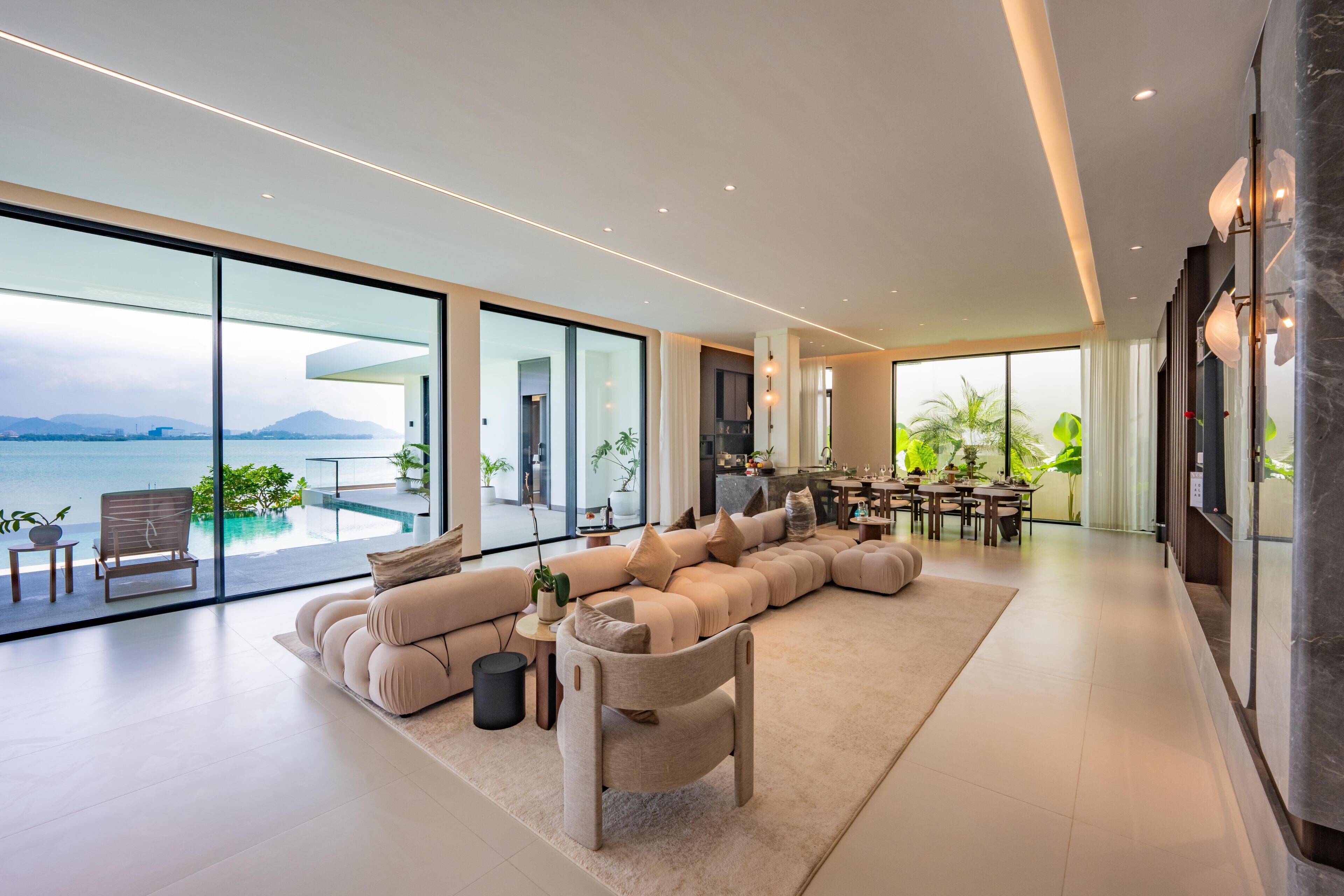 Uma sala de estar ampla com um sofá seccional grande, uma mesa de jantar e vista para o mar.