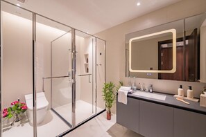 Casa de banho moderna com cabine de duche em vidro, um espelho grande e toucador com artigos de higiene pessoal.