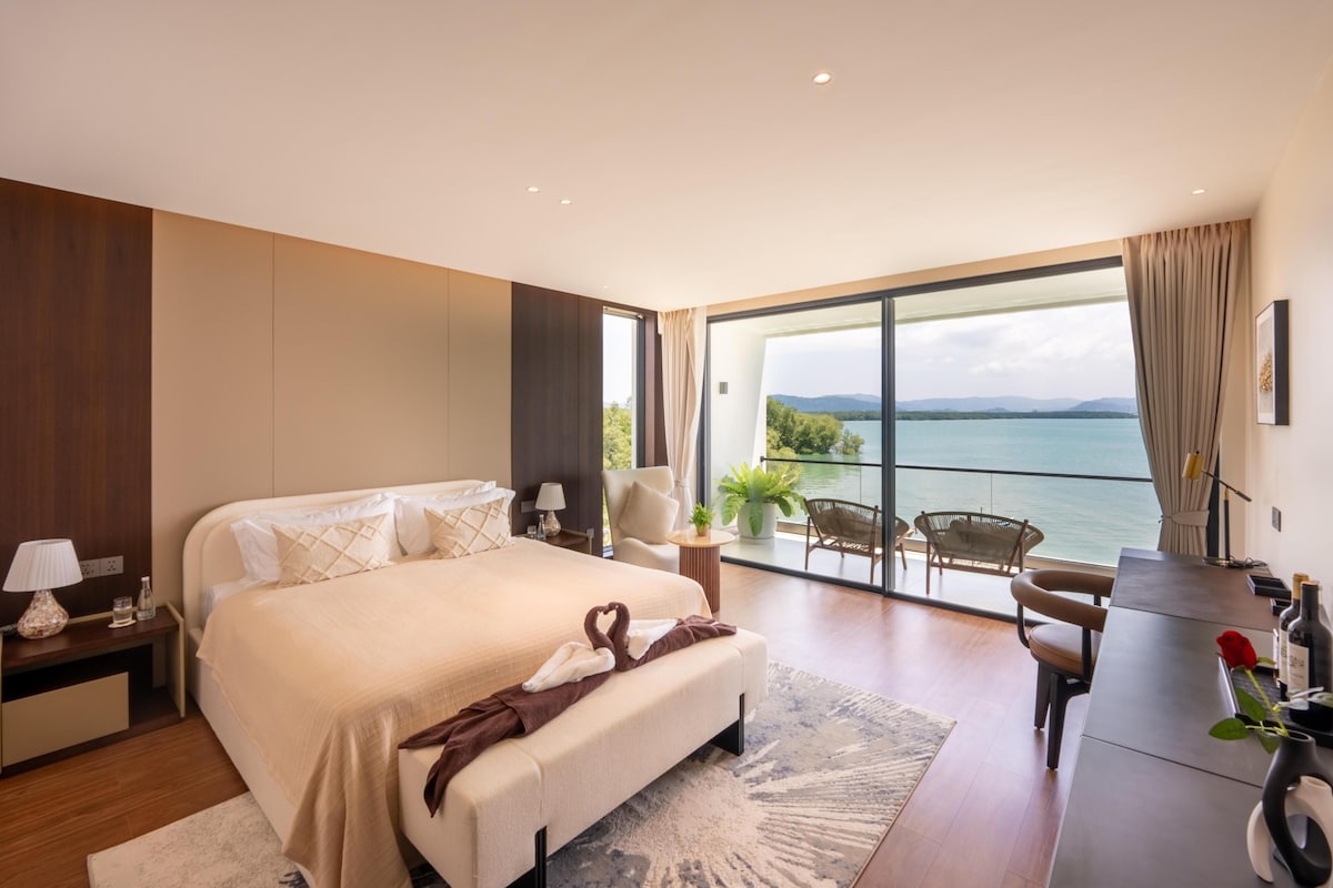 Quarto de hotel moderno com uma cama grande, escrivaninha, cadeira e vista para um lago.
