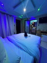 Quarto de hotel com uma cama, televisão de tela plana na parede e uma pequena área de cozinha.