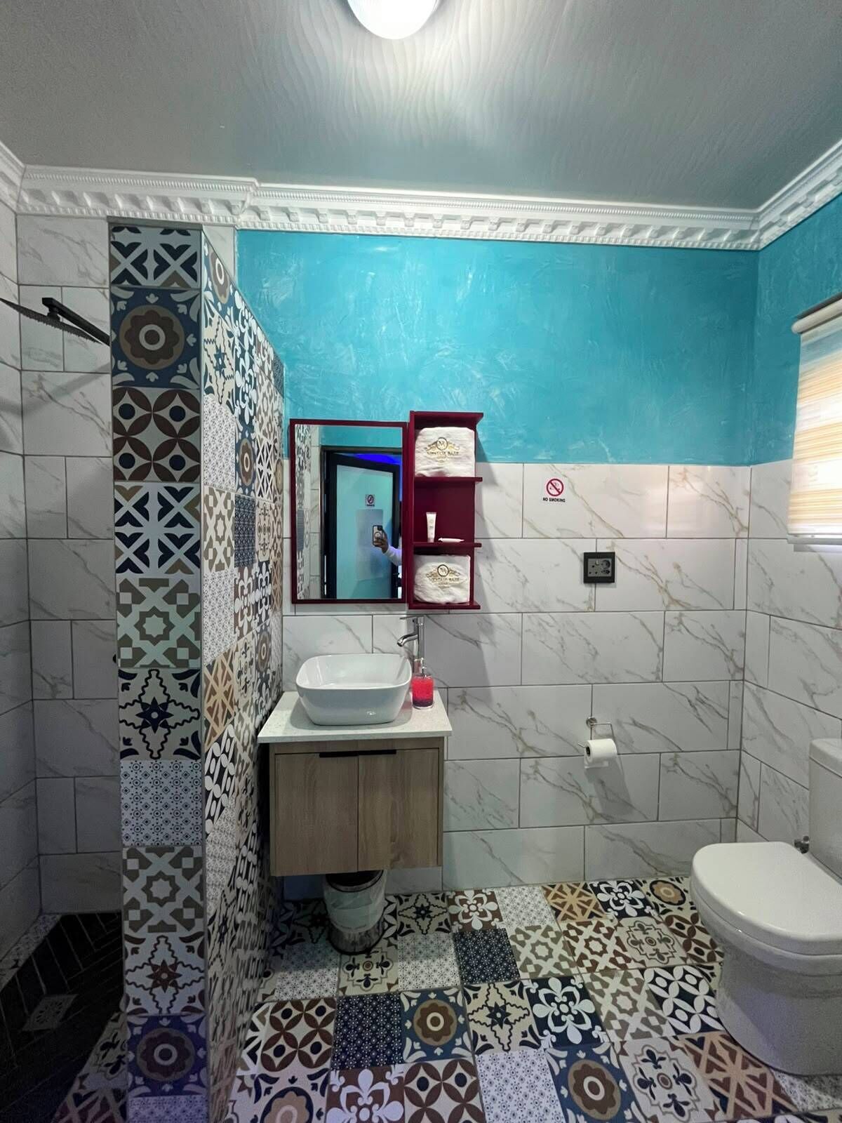 Casa de banho com lavatório branco, espelho, armário vermelho e chão com padrão.
