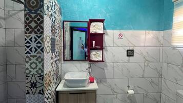 Casa de banho com lavatório branco, espelho, armário vermelho e chão com padrão.
