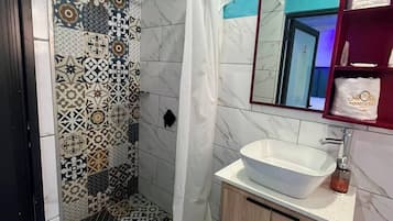 Casa de banho com chuveiro, lavatório e espelho.