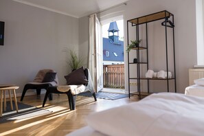 Quarto moderno com cama, uma cadeira, prateleira com toalhas e vista para uma casa através de uma porta aberta.