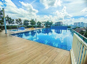 Piscina infinita no terraço com deck de madeira, rodeada por árvores e vista para a cidade.