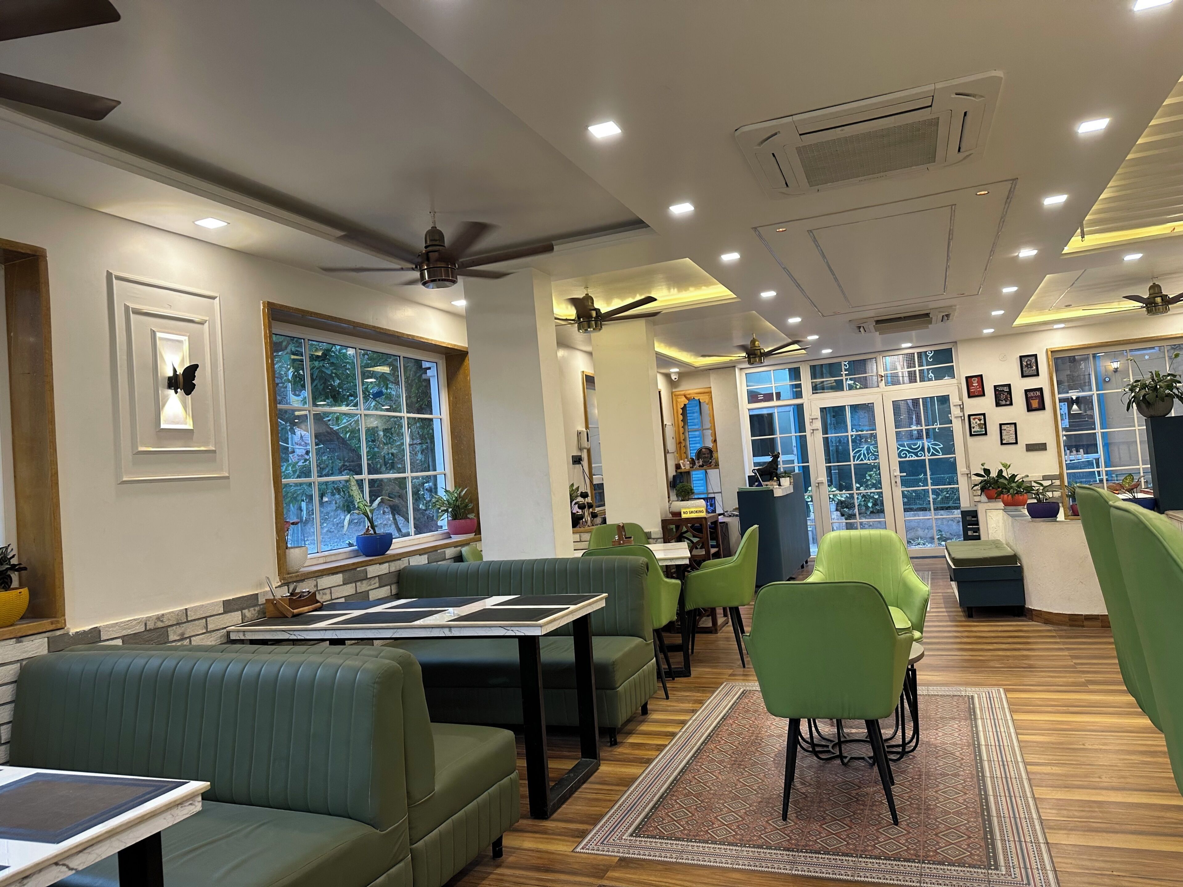 Restaurante com assentos estofados em verde, janelas amplas e ventiladores de teto.