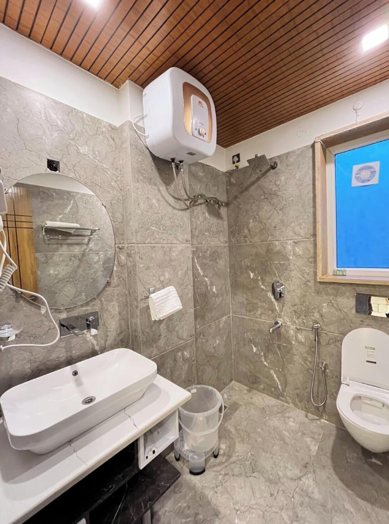 Casa de banho com lavatório branco, chuveiro com chuveiro manual, sanita e toalheiro.