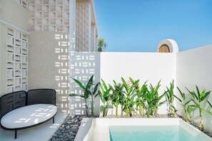 Uma área de estar moderna ao ar livre com piscina, cercada por vegetação e uma parede branca.