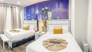 Quarto de hotel com duas camas, uma mesa de cabeceira, abajur e vista para a cidade.