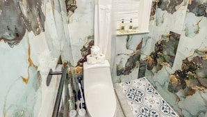 Casa de banho com sanita branca, zona de duche e pequena prateleira com artigos de higiene pessoal.