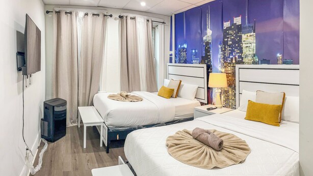Quarto de hotel com duas camas, uma escrivaninha, uma cadeira, uma televisão e um mural com vista para a cidade.