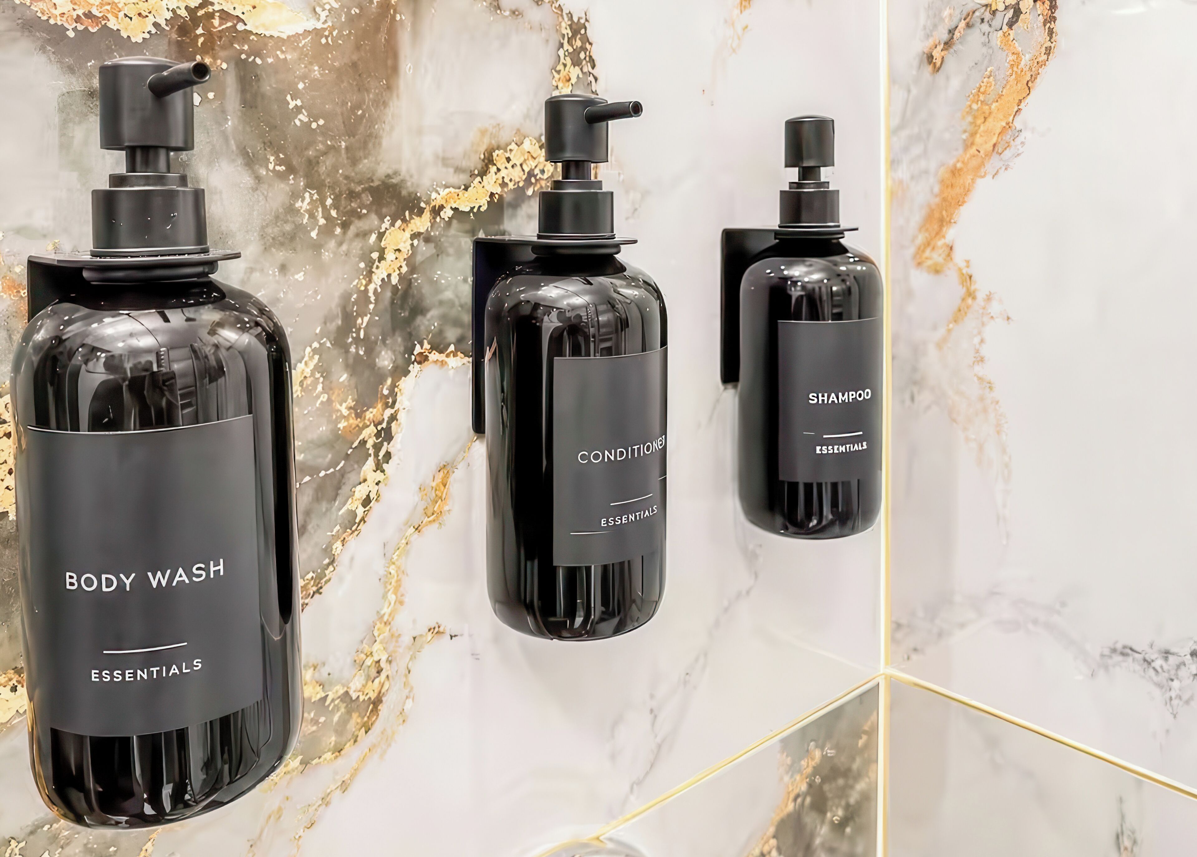 Três frascos pretos de gel de banho e shampoo sobre uma parede de mármore com detalhes dourados.
