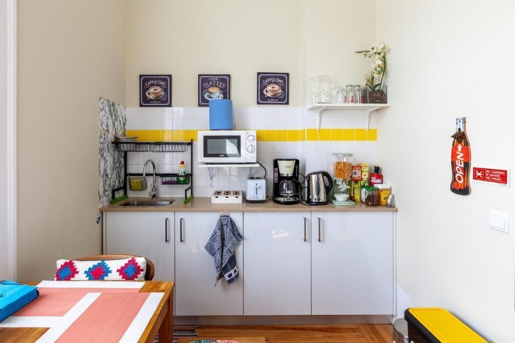 Cozinha compacta com micro-ondas, torradeira, cafeteira e diversos utensílios de cozinha na bancada.