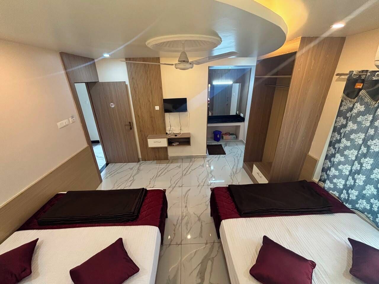 Quarto de hotel com duas camas, televisão, ventoinha no teto e banheiro visível por uma porta aberta.