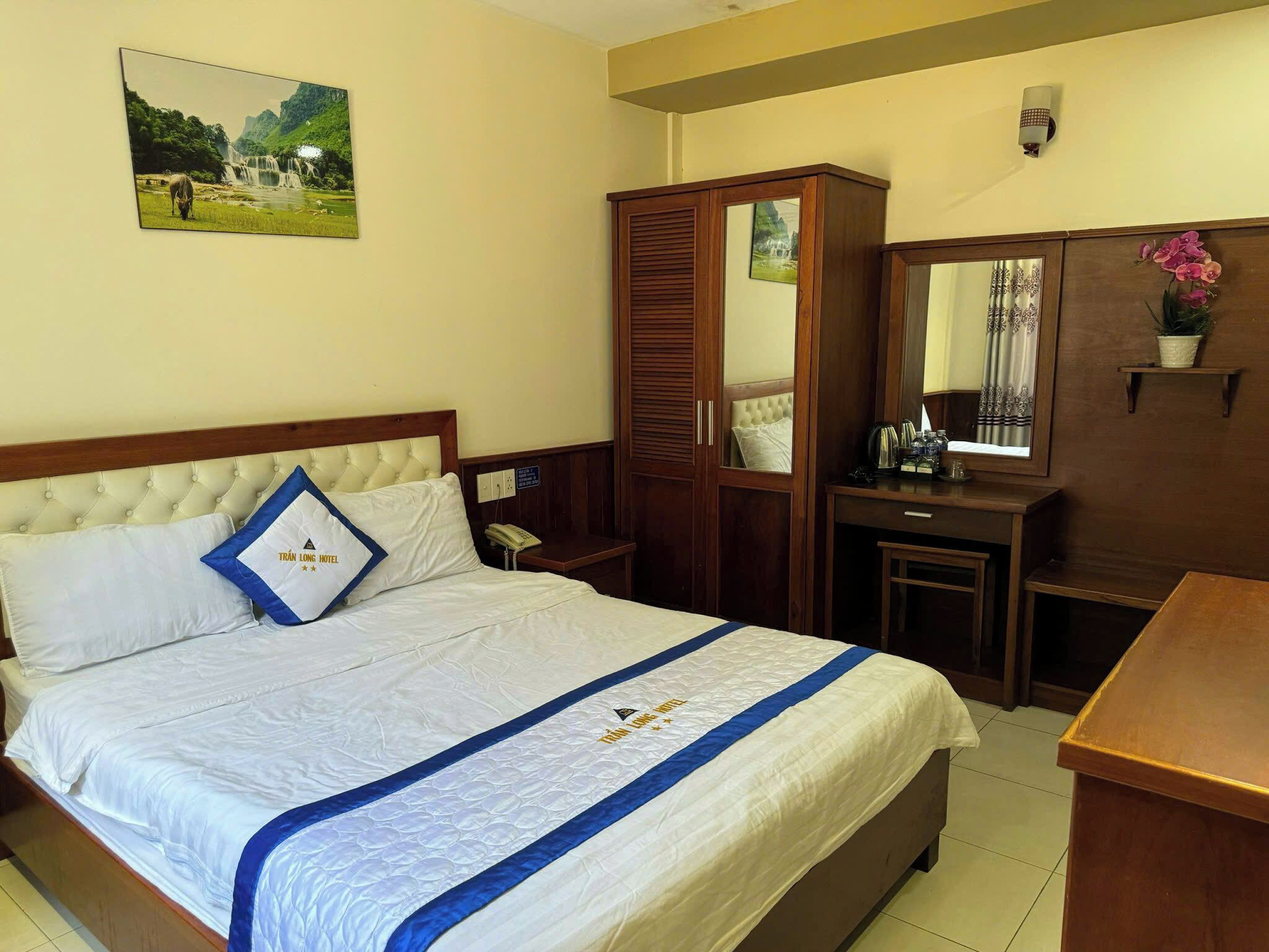 Quarto de hotel com cama, guarda-roupa, mesa de cabeceira, espelho e um quadro na parede.