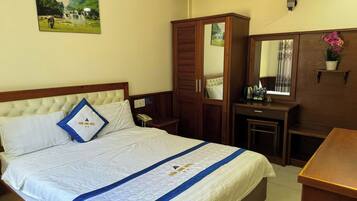 Quarto de hotel com cama, guarda-roupa, mesa de cabeceira, espelho e um quadro na parede.