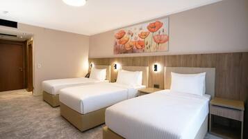 Quarto de hotel com três camas, cabeceira de madeira, pintura de flores e piso coberto por carpete.