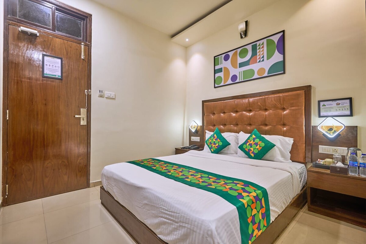 Quarto de hotel com cama grande, porta de madeira, mesa de cabeceira com luminária e obra de arte pendurada na parede.