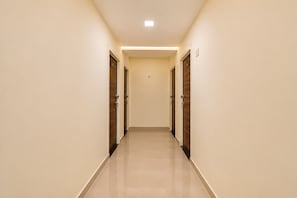 Um corredor com portas em ambos os lados, um luminar no teto e chão de azulejos.