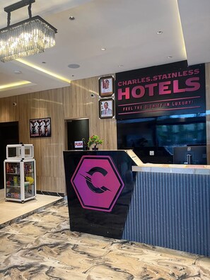 Balcão de recepção de hotel com um logotipo em destaque, um candelabro e uma placa para Charles Stainless Hotels.