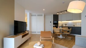 Uma sala de estar moderna com uma televisão de tela plana, uma mesa de centro de madeira e uma área de jantar com mesa e cadeiras.