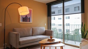 Uma sala de estar moderna com sofá, mesa de centro, abajur e uma janela grande com vista para a cidade.