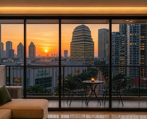 Varanda com vista para a cidade ao pôr do sol, com sofá, duas cadeiras e uma mesinha com vela.