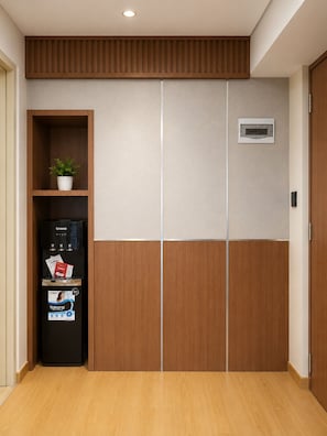 Quarto com guarda-roupa de madeira, dispensador de água e uma pequena estante com uma planta.