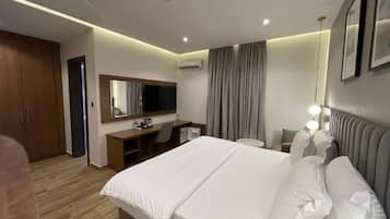 Quarto de hotel com cama, escrivaninha, cadeira, televisão e armário.