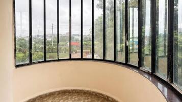 Quarto com parede curva e grandes janelas, com vista para áreas verdes e edifícios.