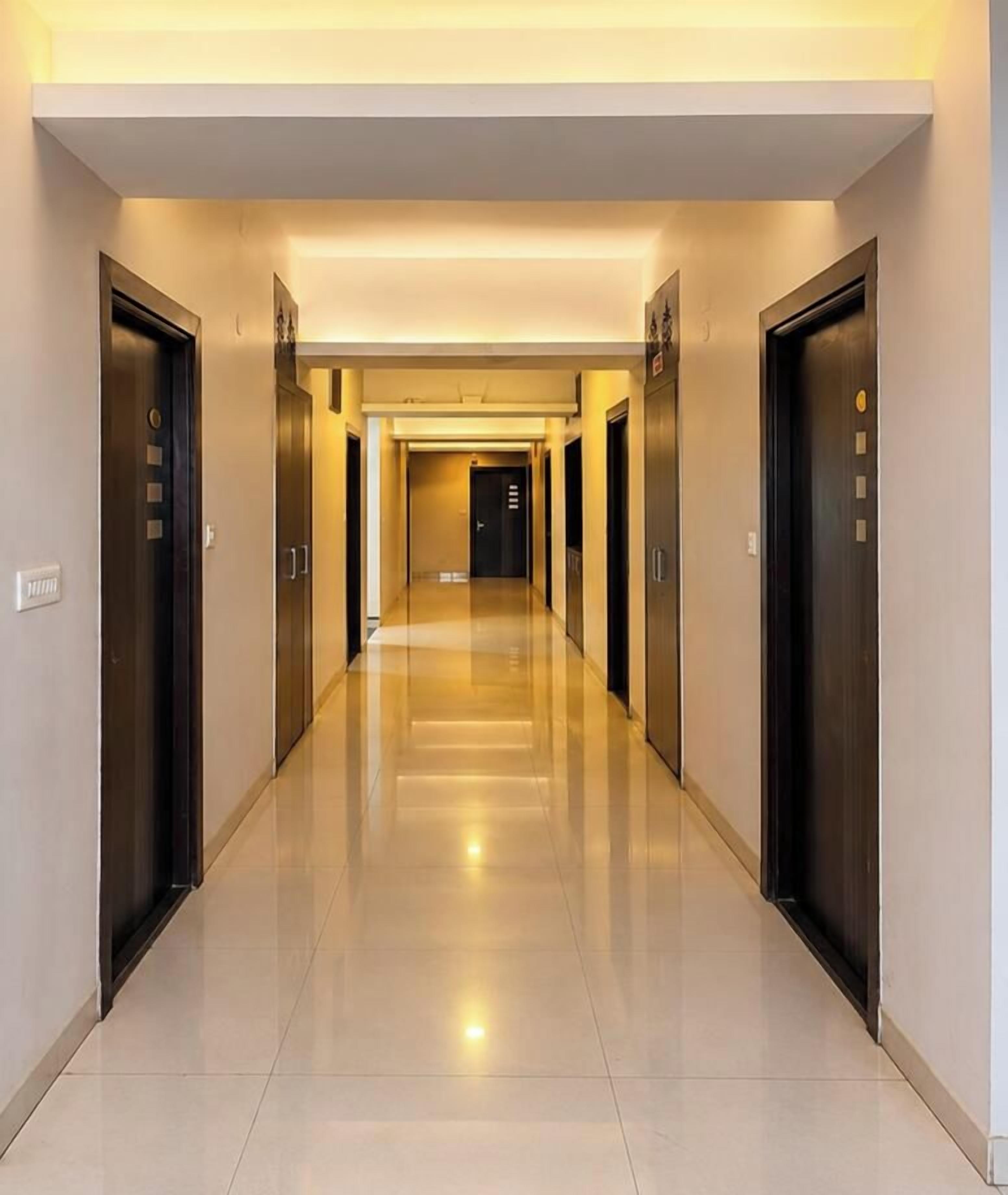 Um corredor longo e bem iluminado, com portas alinhadas em ambos os lados, dando acesso a quartos.