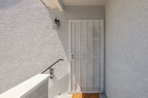 Uma porta branca com grades de metal, uma pequena luminária externa e uma fechadura de metal.