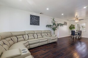 Uma sala de estar moderna com sofá seccional, mesa de jantar com cadeiras e ventilador de teto.