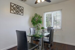 Uma sala de jantar com mesa de vidro, quatro cadeiras, planta em vaso e janela com persianas.
