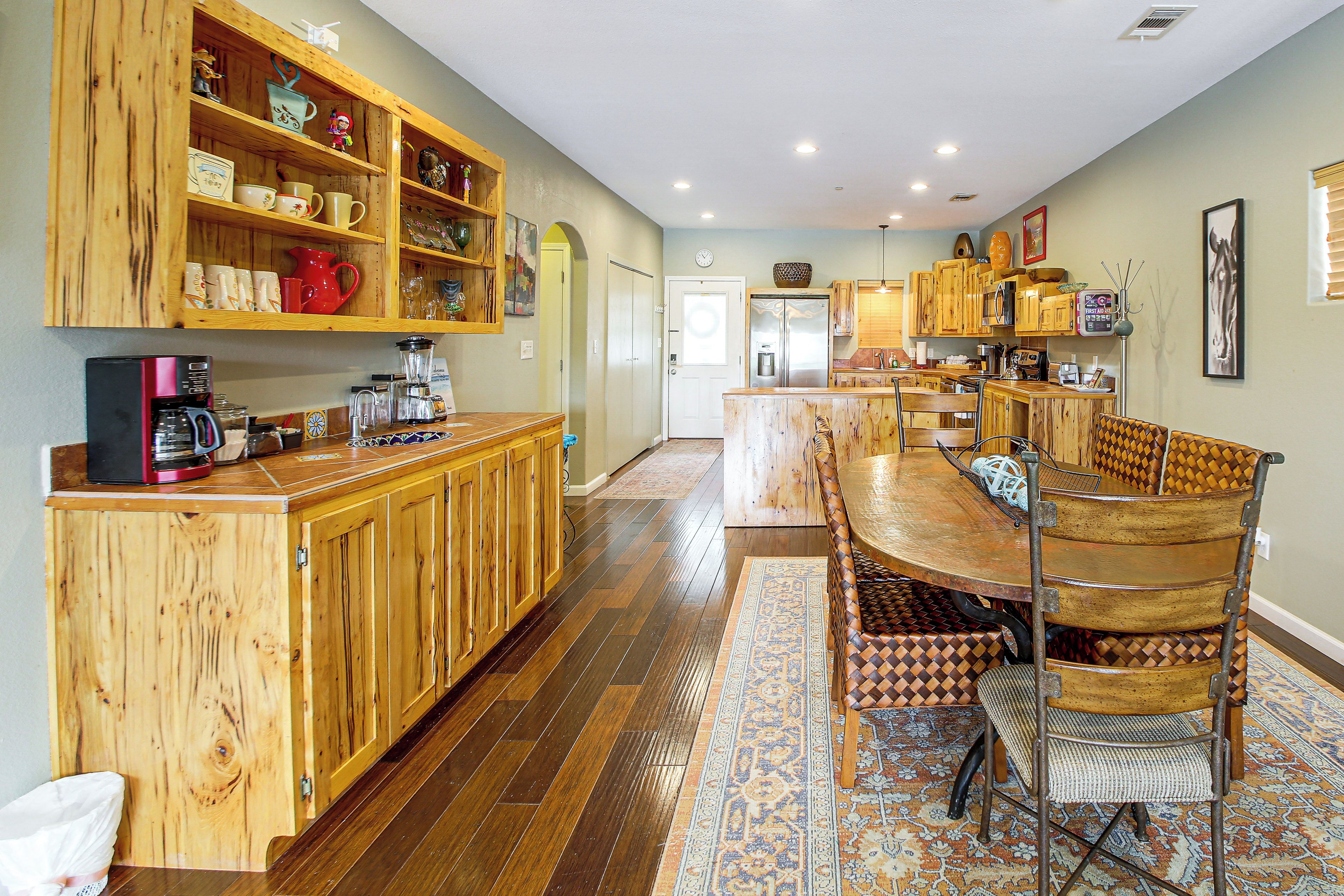 Cozinha com armários de madeira, cafeteira e área de jantar com cadeira de vime e mesa.