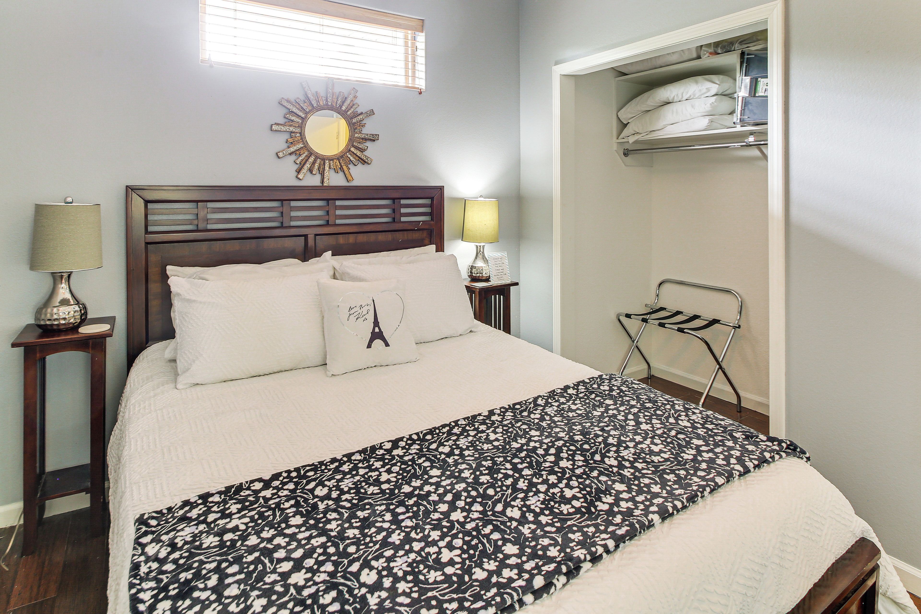 Cama bem arrumada com colcha estampada em flor, cabeceira com espelho decorativo e mesa de cabeceira com abajur.
