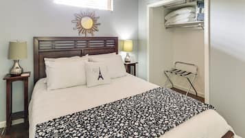 Cama bem arrumada com colcha estampada em flor, cabeceira com espelho decorativo e mesa de cabeceira com abajur.