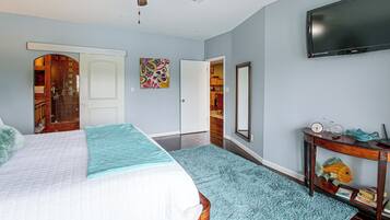 Quarto com cama, ventoinha no teto, televisão e porta que dá para um banheiro.