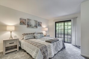 Quarto com uma cama grande, duas mesas de cabeceira e uma janela com vista para árvores.