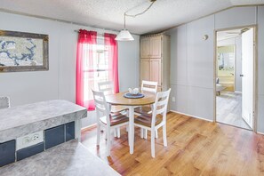Uma área de refeições com uma mesa de madeira e cadeiras brancas, um mapa na parede e vista para a cozinha.