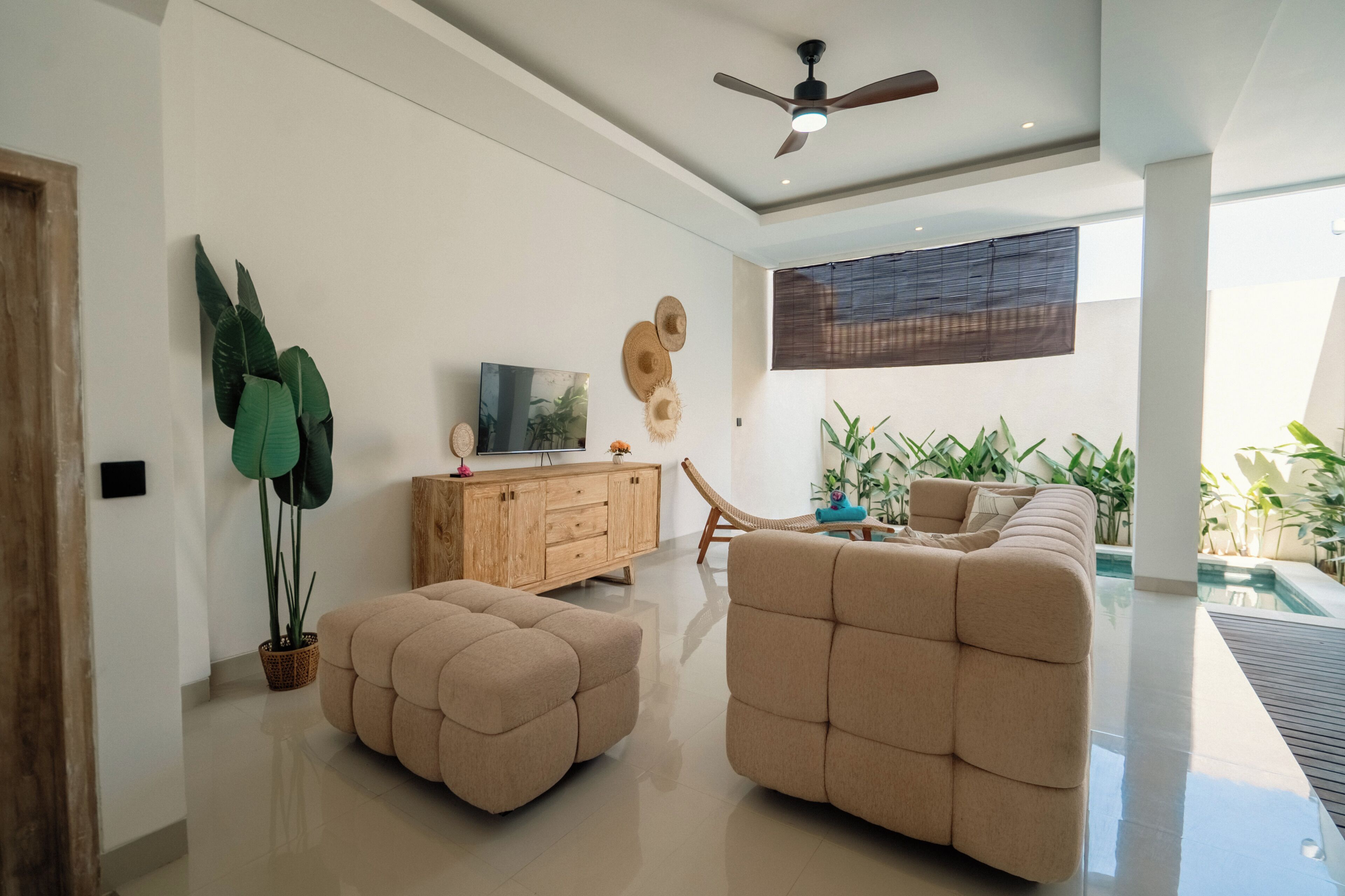 Uma sala de estar moderna com sofá, banquinho, armário de madeira, televisão e decoração na parede.