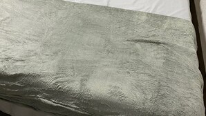 Cama com cobertor cinza e duas almofadas, cabeceira cinza e porta de persiana azul.