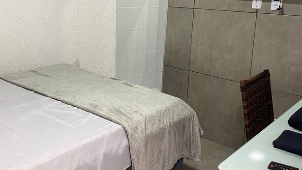 Quarto de hotel com cama, televisão na parede, cadeira e mesa com controle remoto.