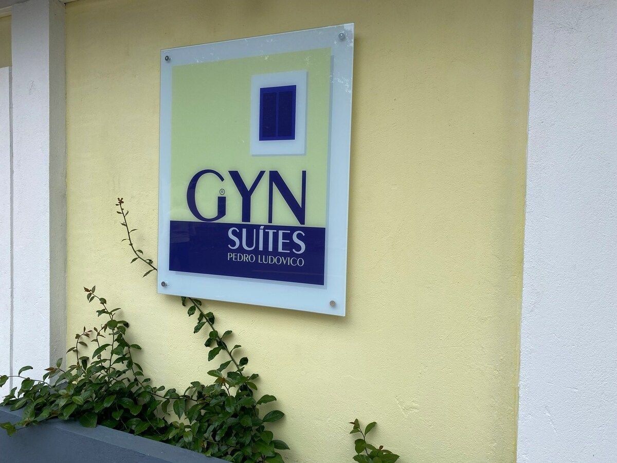 Placa com a inscrição 'GYN SUITES PEDRO LUDOVICO' em uma parede amarela.