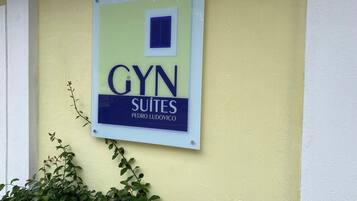 Placa com a inscrição 'GYN SUITES PEDRO LUDOVICO' em uma parede amarela.
