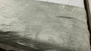 Uma cama com cabeceira cinza, roupa de cama branca e manta cinza.